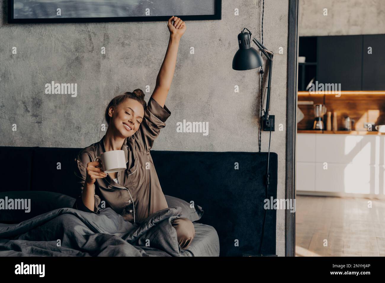 Sleepy relaxed lovely girl in satin pajama trying to wake up from night ...