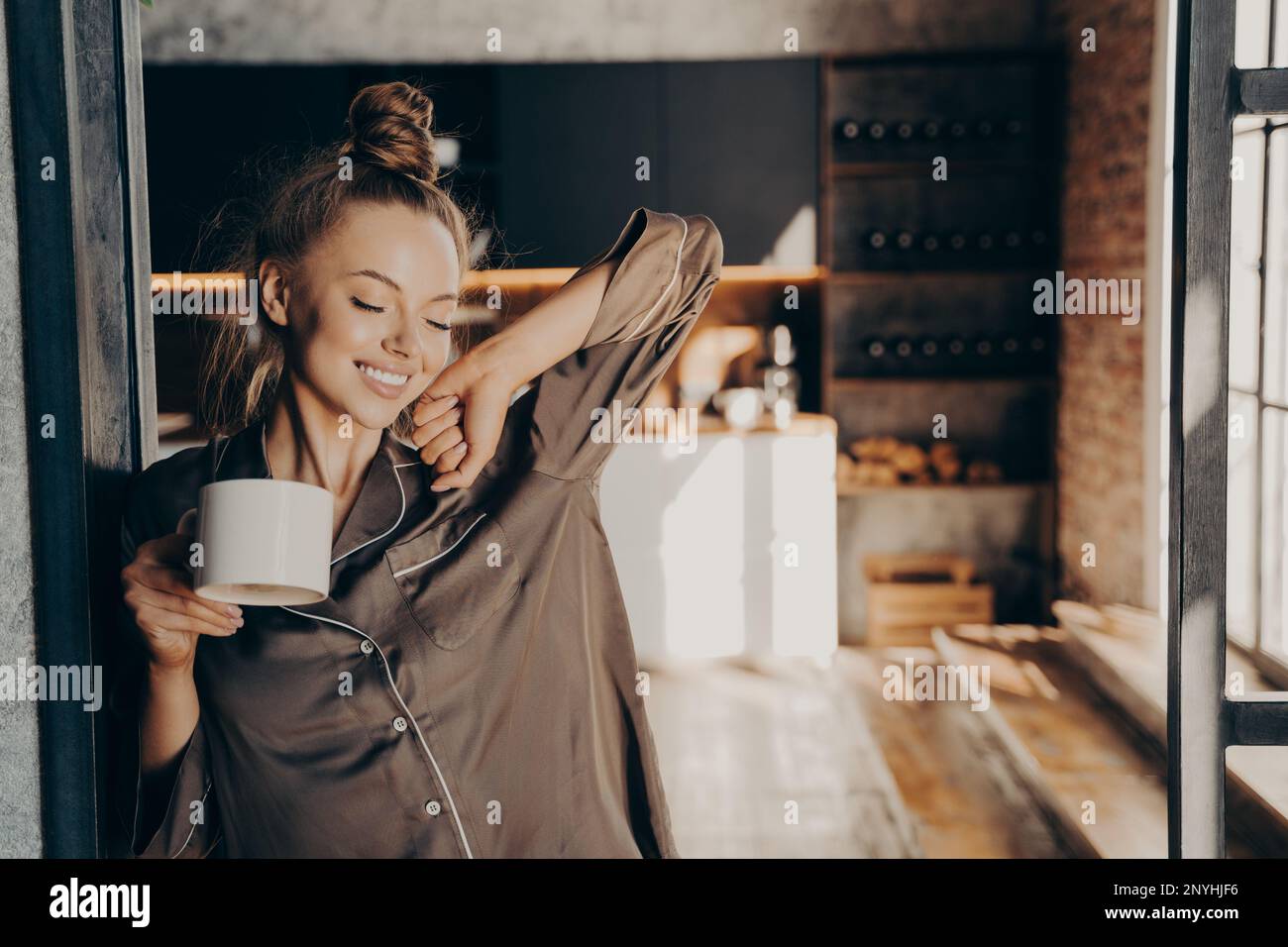 New day. Happy beautiful brunette female stretching with cup of coffee ...
