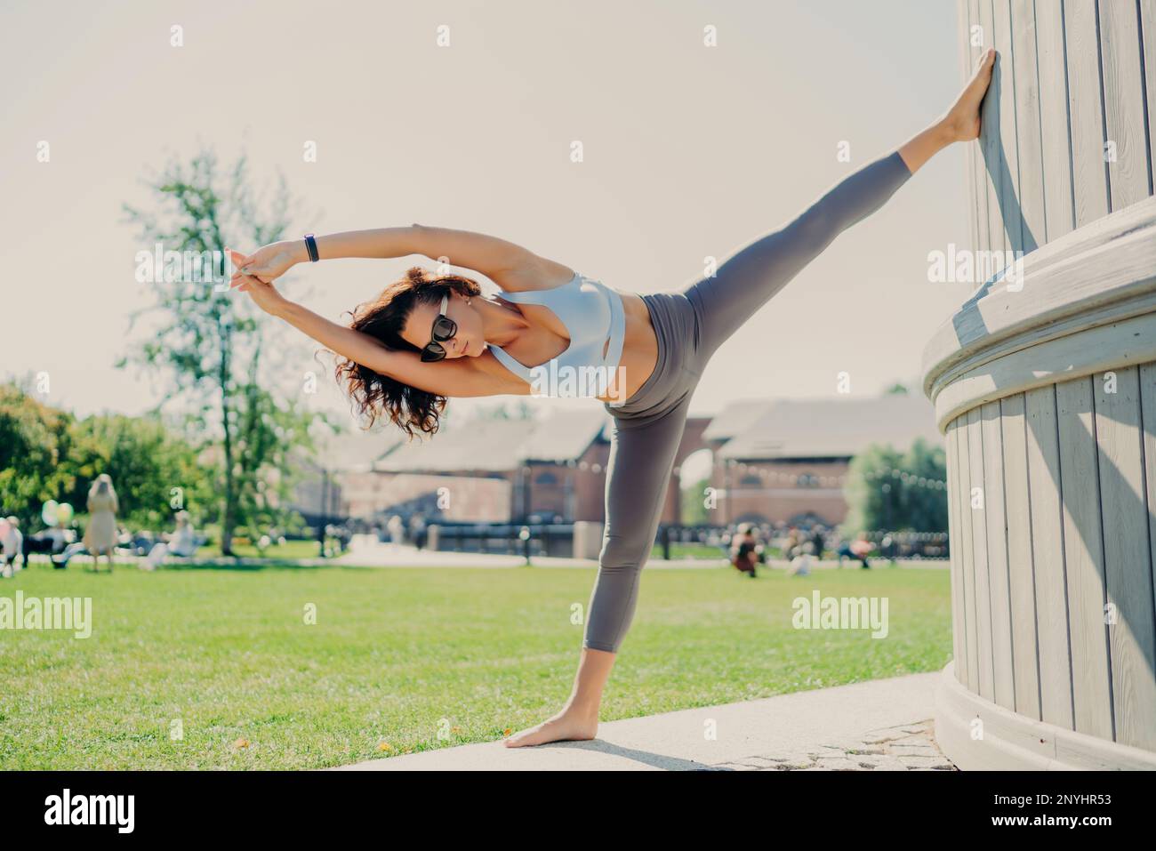 Horizontal shot of flexible fit woman stands on one leg leans with arms ...