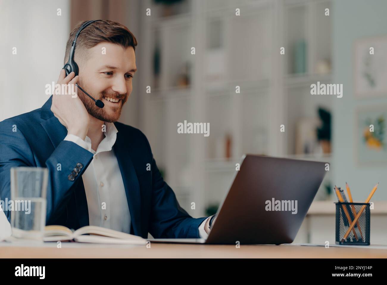 Side view of happy businessman wearing suit using laptop and headset ...