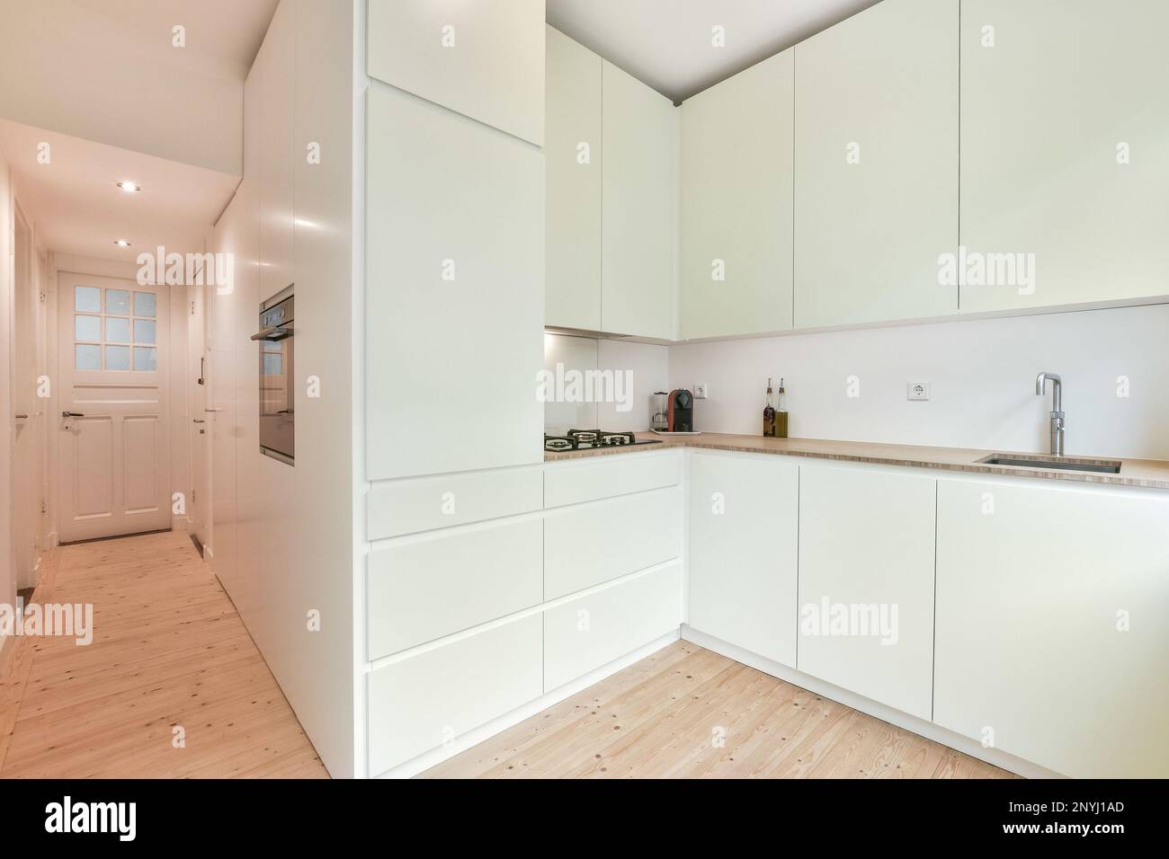 a kitchen with white cupboards and wood flooring in an apartment, taken ...