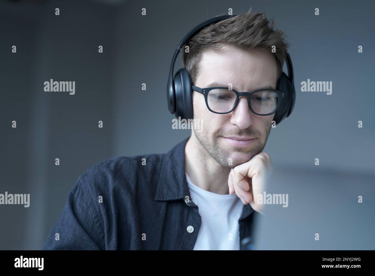 Smiling german man in glasses wearing headphones looking on screen of ...