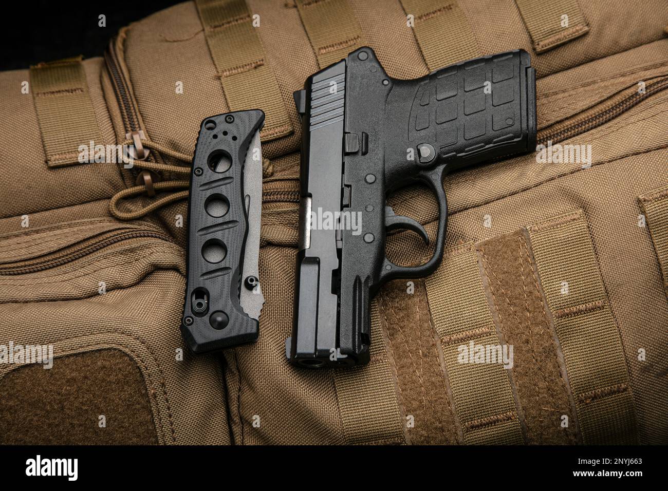 A small modern pistol and penknife on a brown military backpack. Self ...