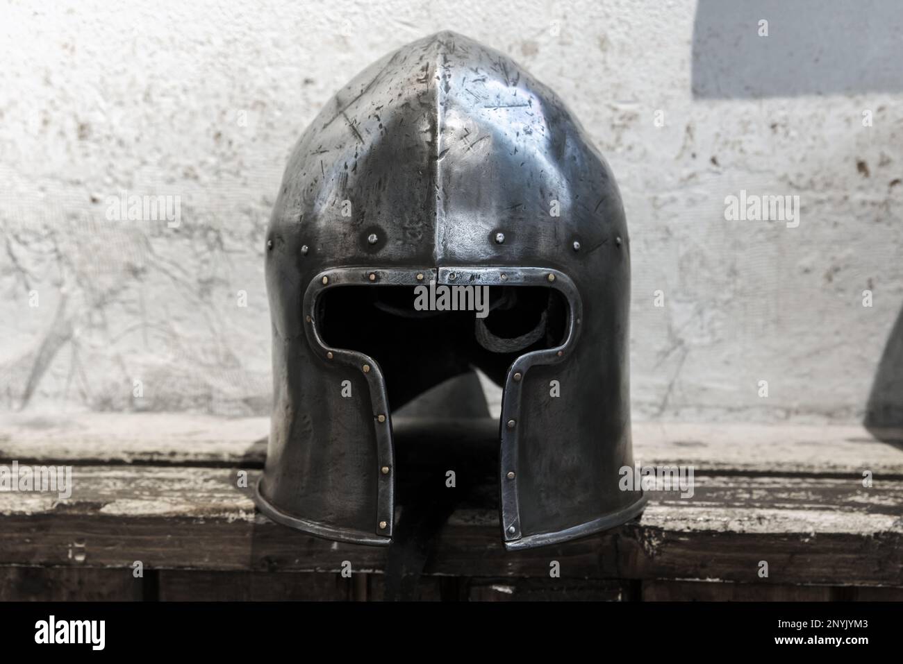 Steel helmet of medieval knight lays on a rough wooden shelf in front ...