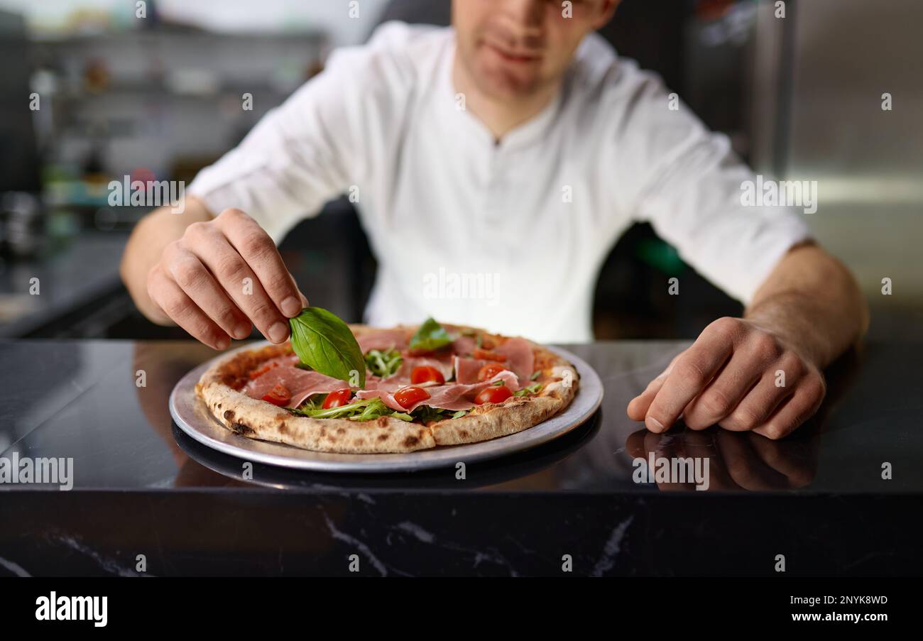 Chef pizzaiolo decorating pizza with fresh oregano leaves Stock Photo ...