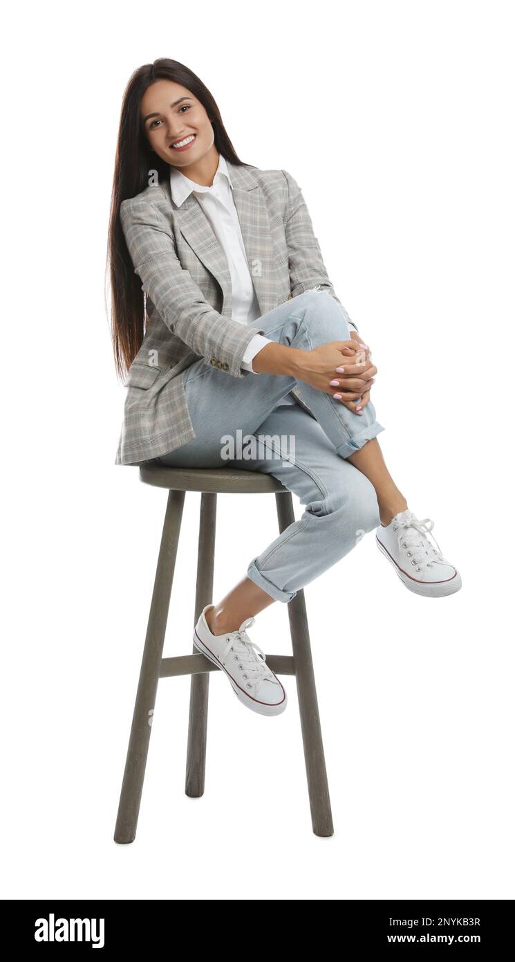 Beautiful young woman sitting on stool against white background Stock ...