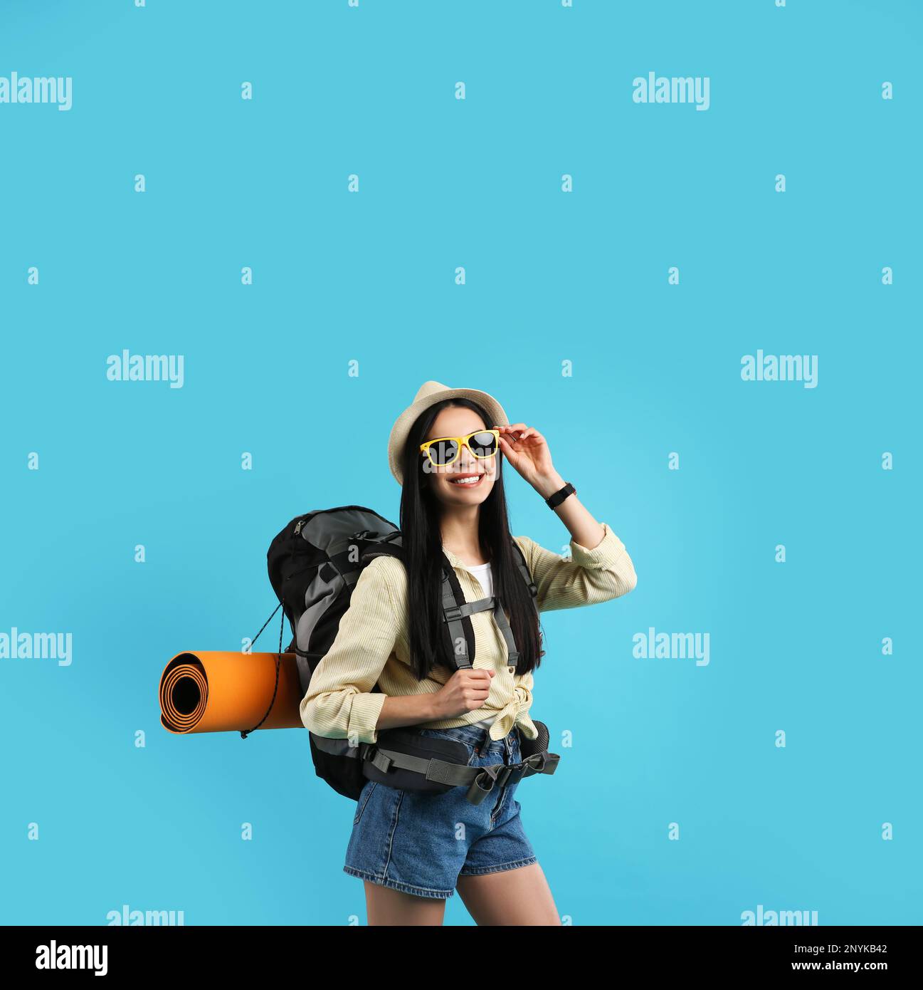 Happy female tourist with backpack on light blue background Stock Photo ...