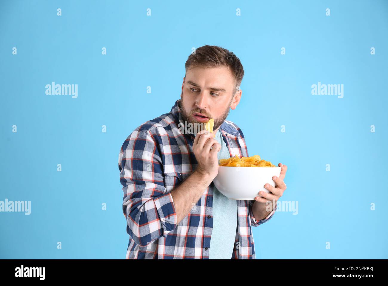 Greedy young man hiding bowl with chips on light blue background Stock ...
