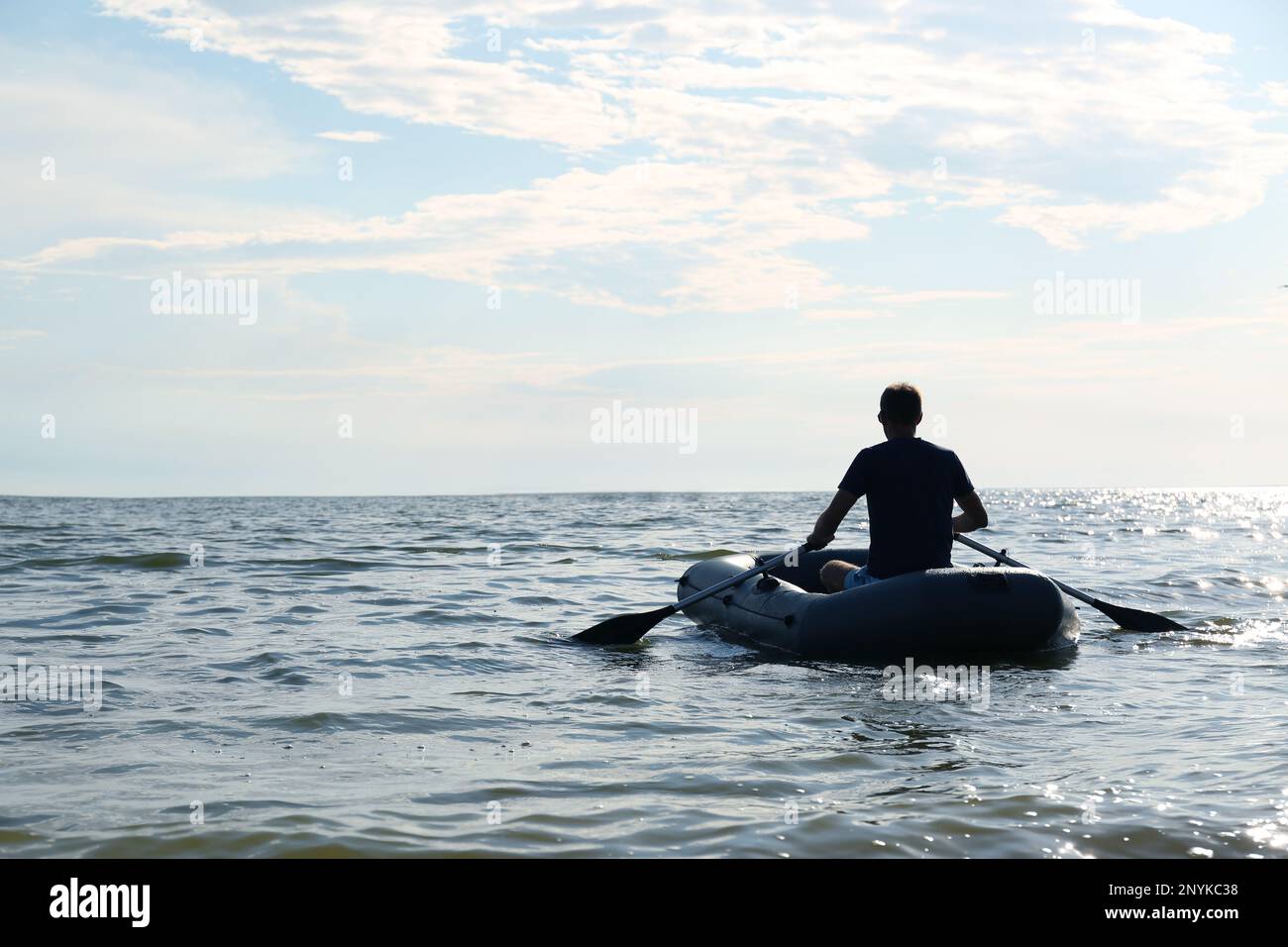 Man rowing inflatable rubber fishing boat on sea, back view. Space for ...