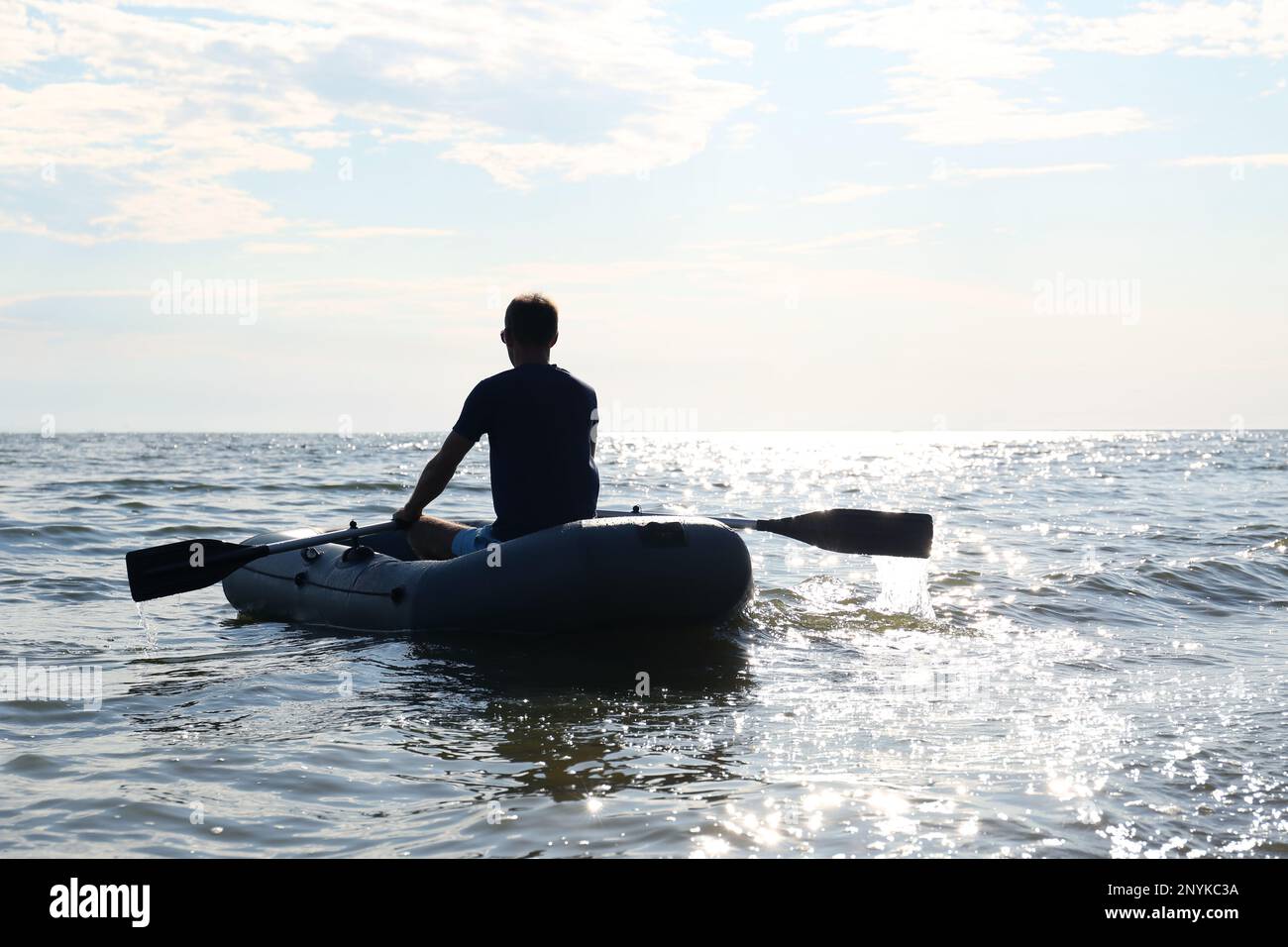 Man rowing inflatable rubber fishing boat on sea, back view. Space for ...