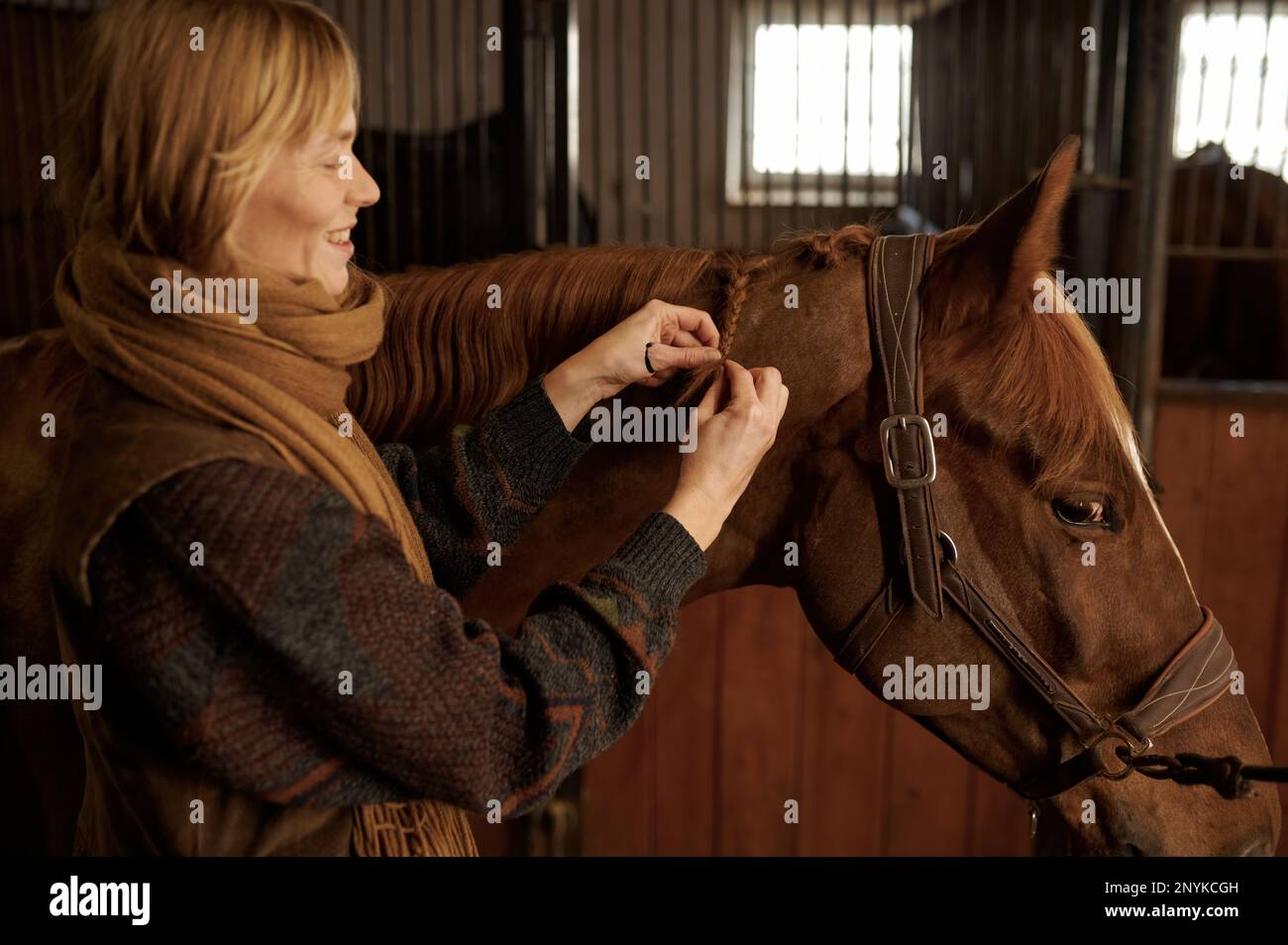 Portrait of woman braiding horse mane while standing in stable of ...