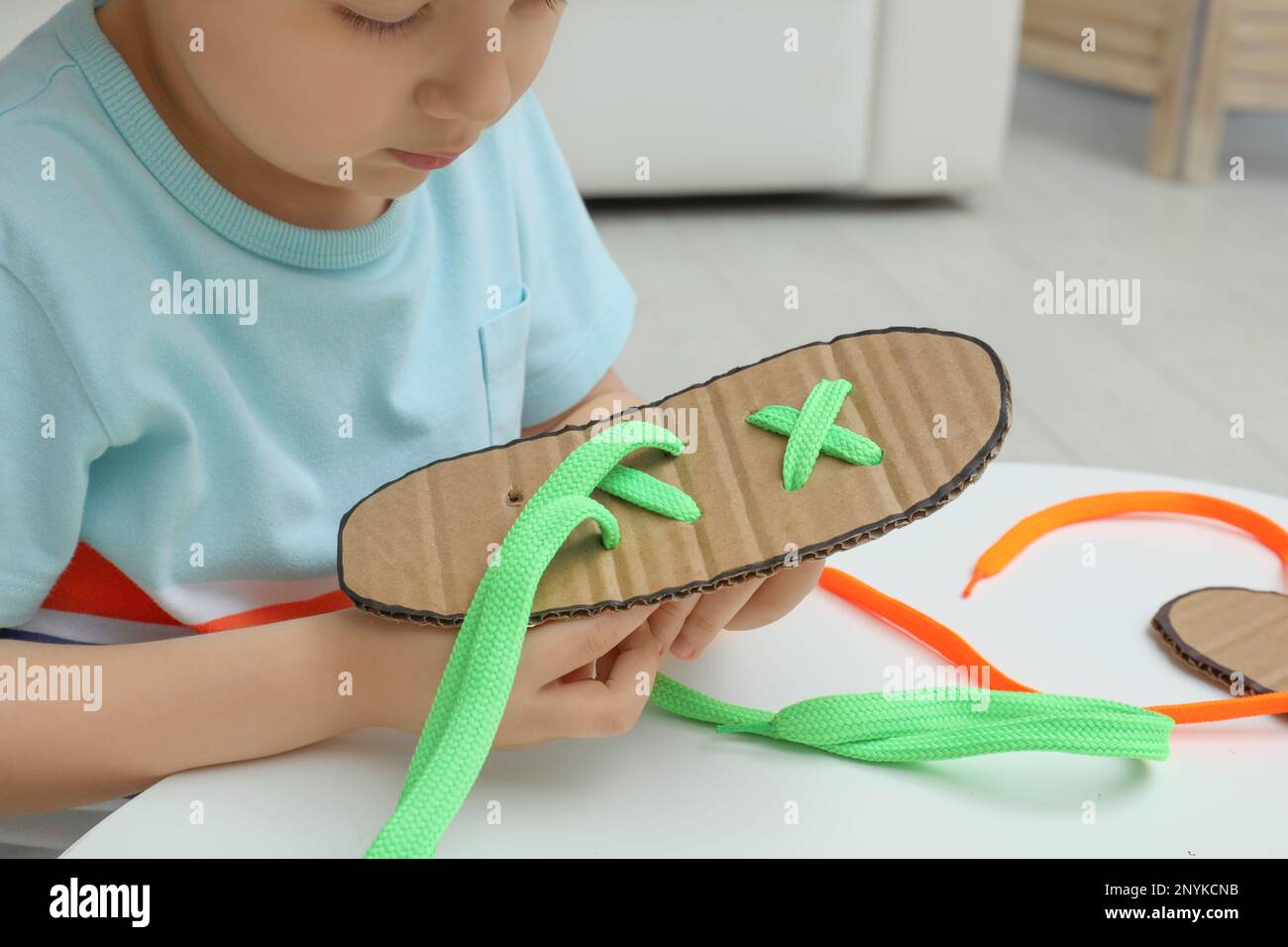 Little boy tying shoe lace using training cardboard template at white ...
