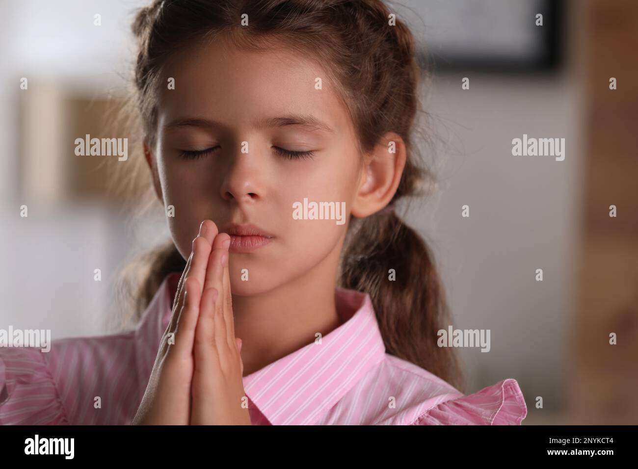 Cute little girl with hands clasped together praying at home Stock ...