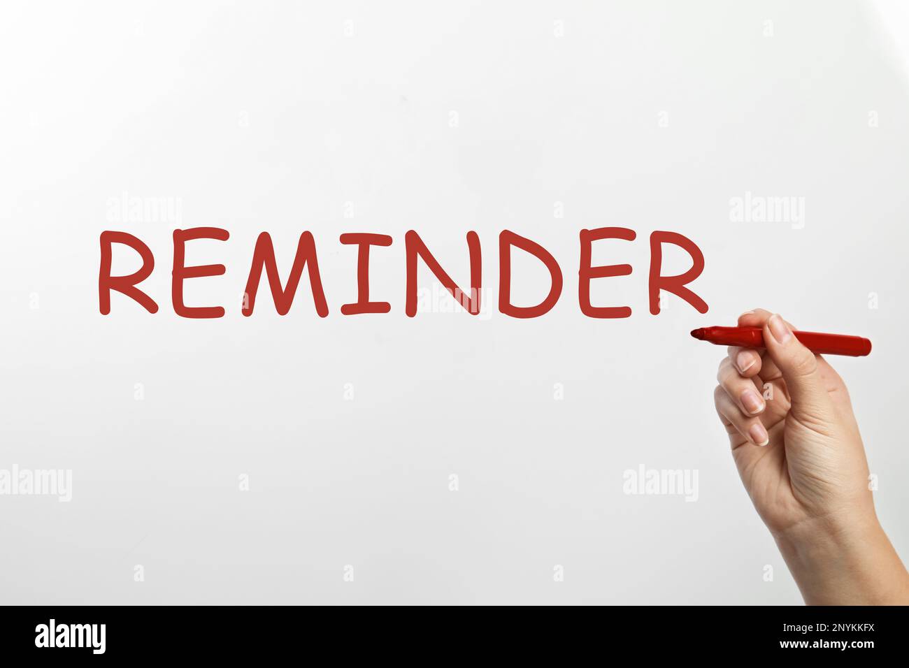 Woman writing word REMINDER on glass against white background, closeup ...