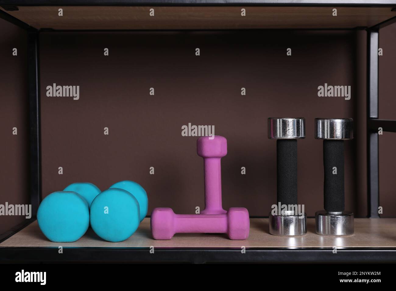 Different dumbbells on shelf near brown wall. Sports equipment Stock ...