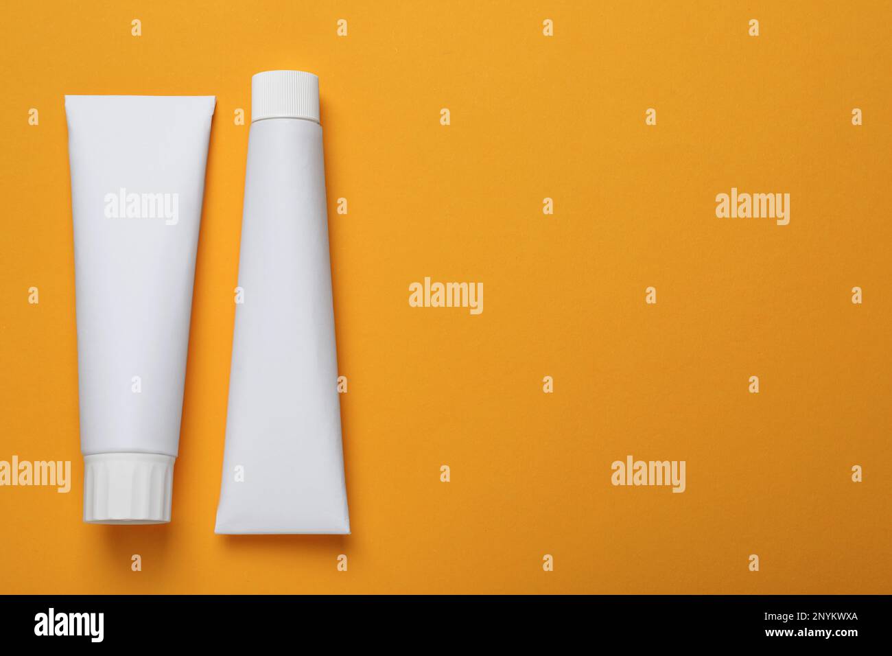 Blank tubes of toothpaste on orange background, flat lay. Space for ...