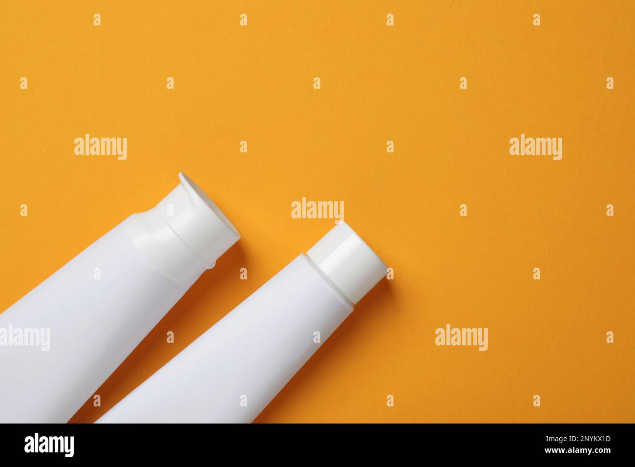 Blank tubes of toothpaste on orange background, flat lay. Space for ...