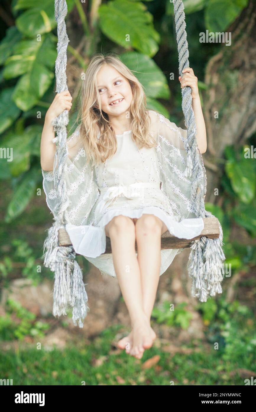 Little blond girl barefoot in dreamy white flower girl dress on tree ...