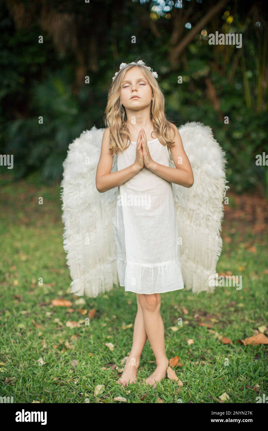 Little girl barefoot in white dress with angel wings and flower crown ...