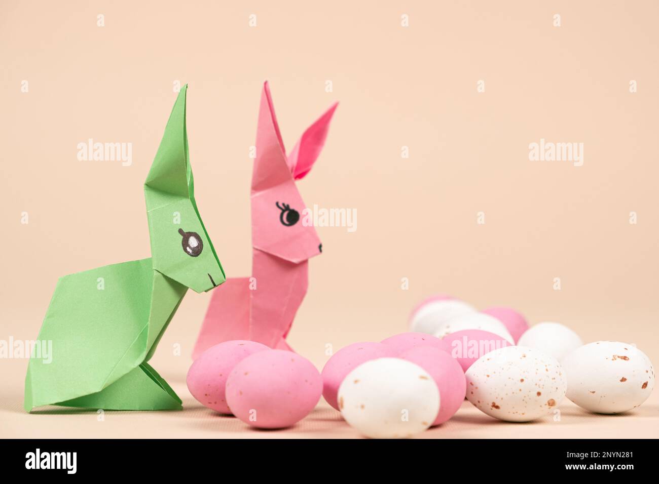 Two paper origami bunnies and an Easter egg on a beige background ...