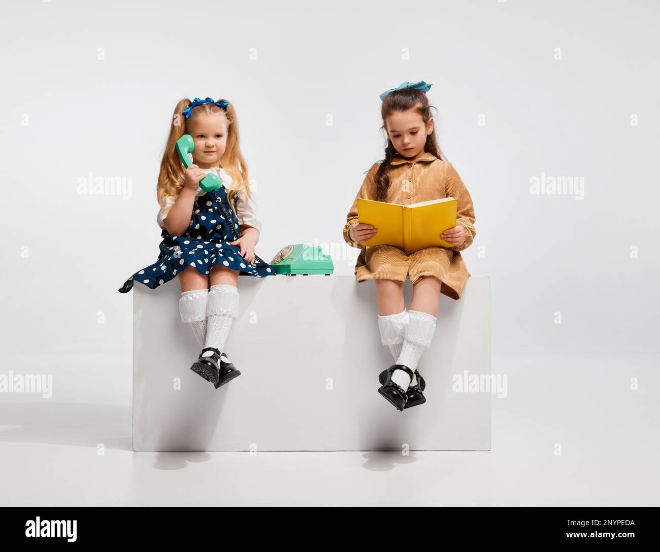 Calm kids. Two beautiful stylish little girls sitting, talking on phone ...