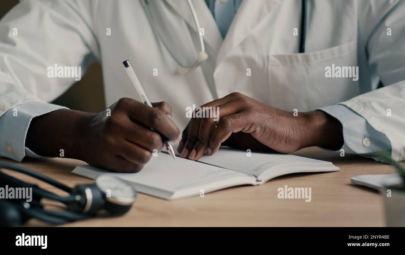 Unknown male hands african man doctor sit at clinic desk writing ...