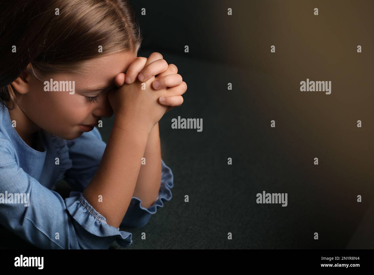 Cute little girl praying on dark green background, closeup. Space for ...