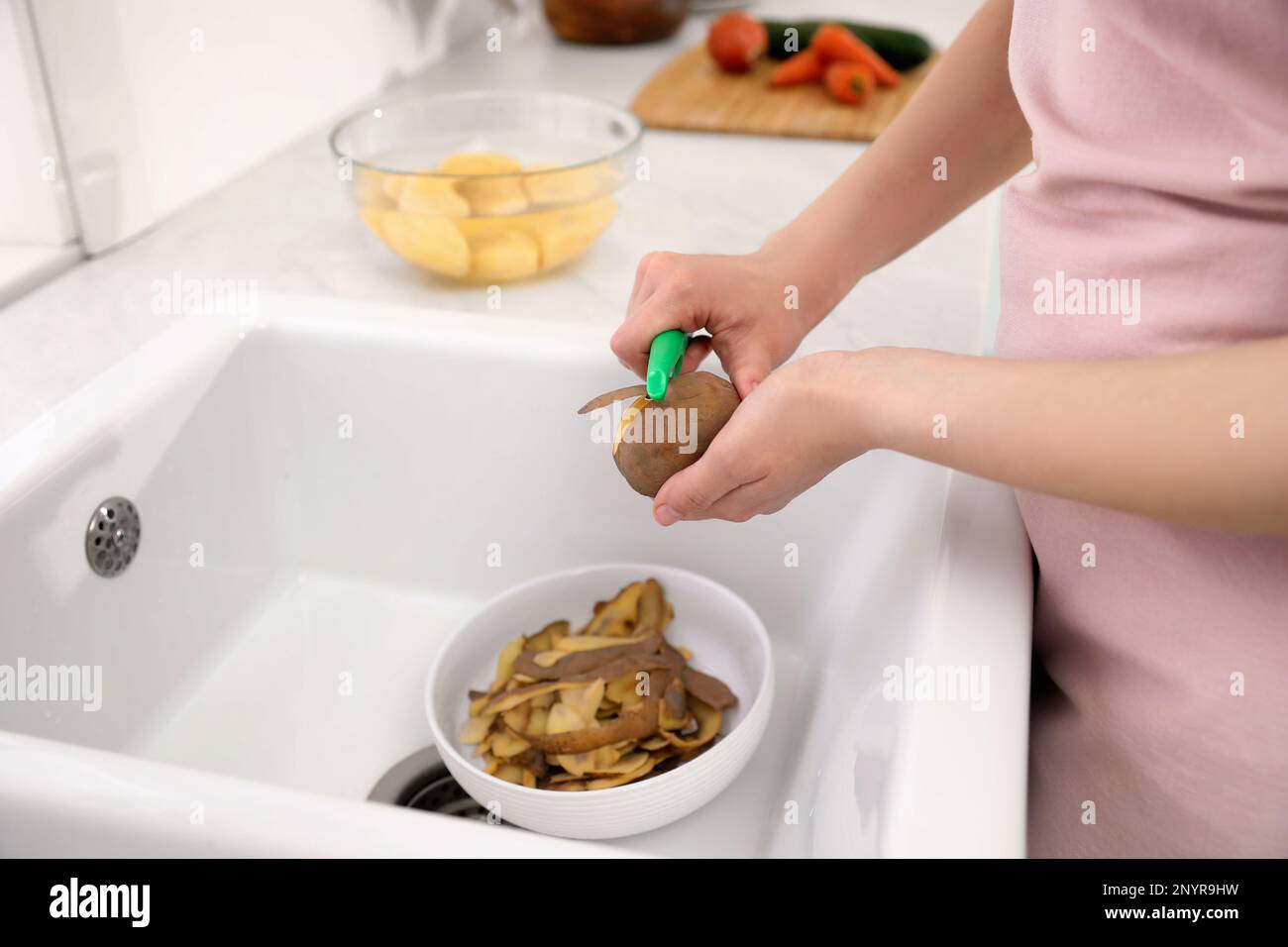 Woman peeling potato near kitchen sink, closeup. Preparing vegetable ...