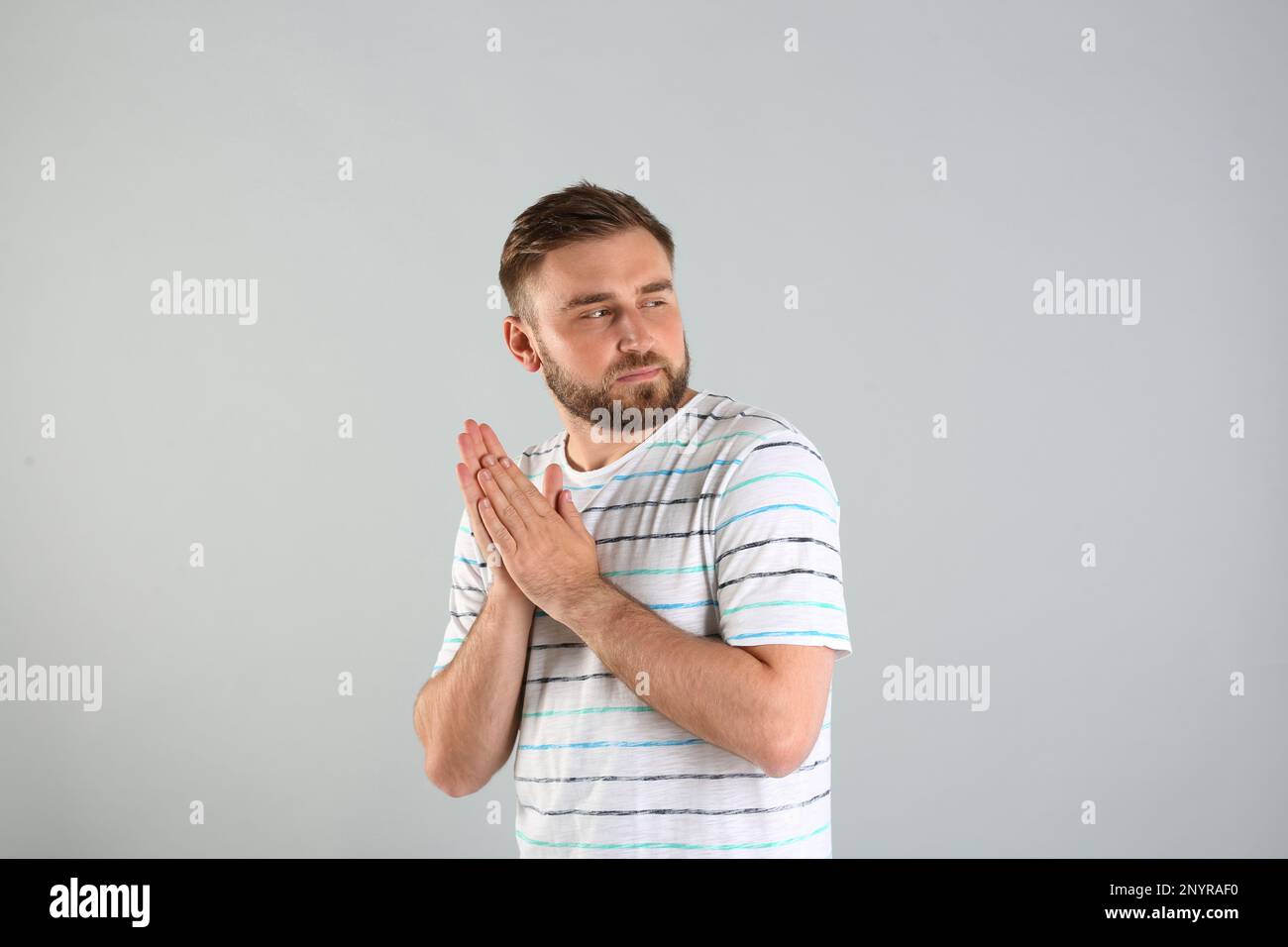 Greedy young man rubbing hands on light grey background Stock Photo - Alamy