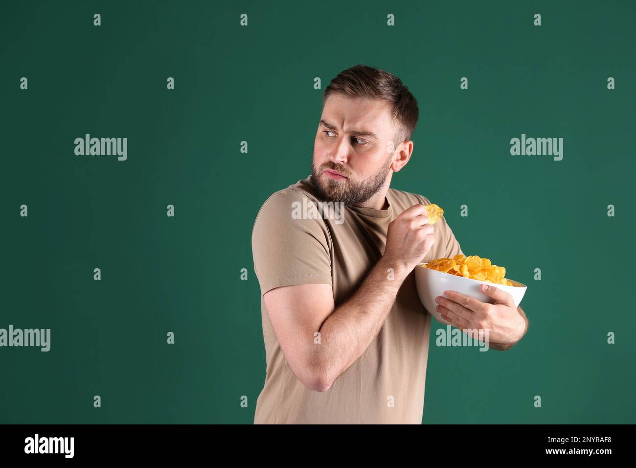 Greedy young man hiding bowl with chips on green background Stock Photo ...