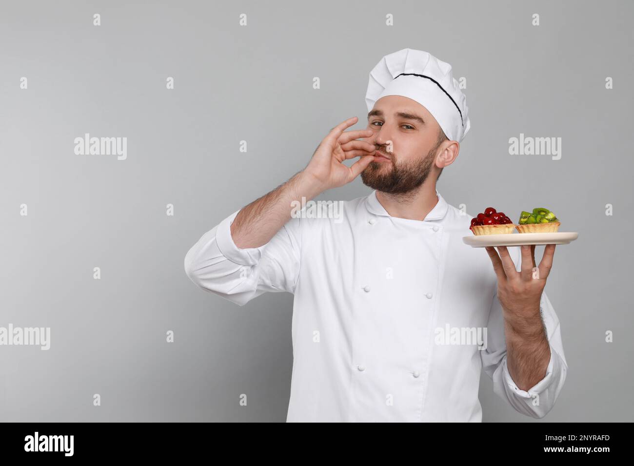 Happy professional confectioner in uniform with tartlets showing ...