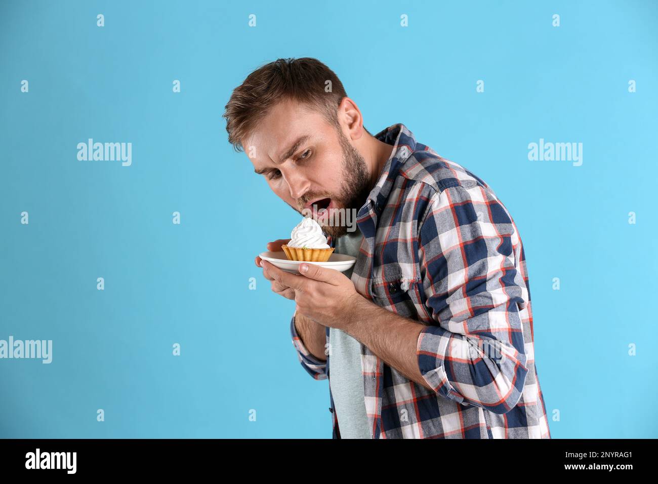Greedy young man hiding cupcake on light blue background, space for ...