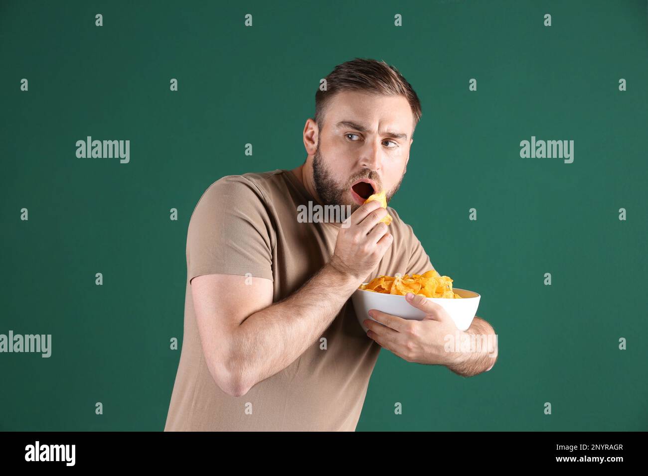 Greedy young man hiding bowl with chips on green background Stock Photo ...