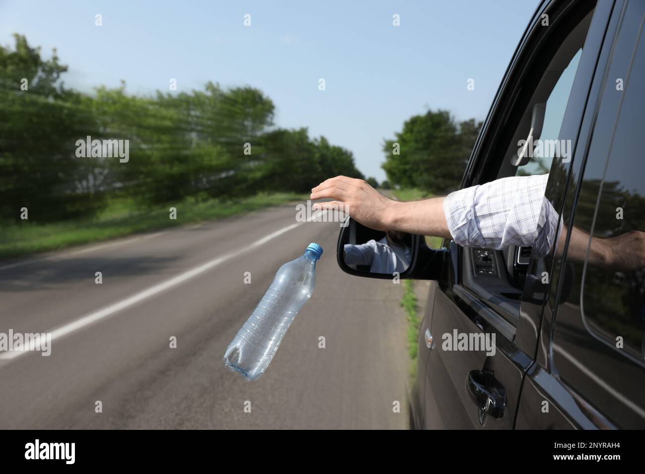 Driver throwing away plastic bottle from car window. Garbage on road ...