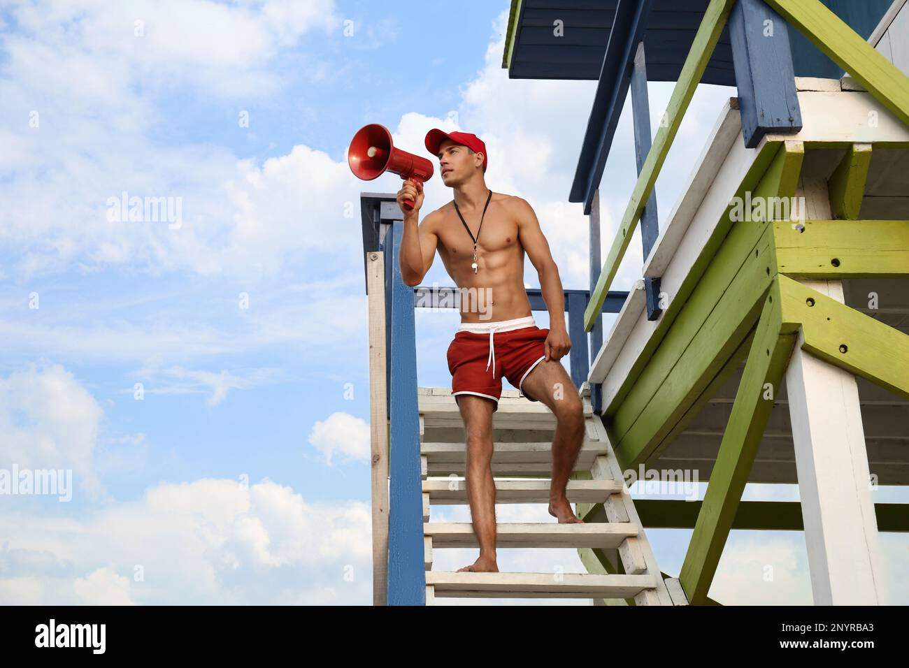 Handsome lifeguard with megaphone on watch tower against sky Stock ...