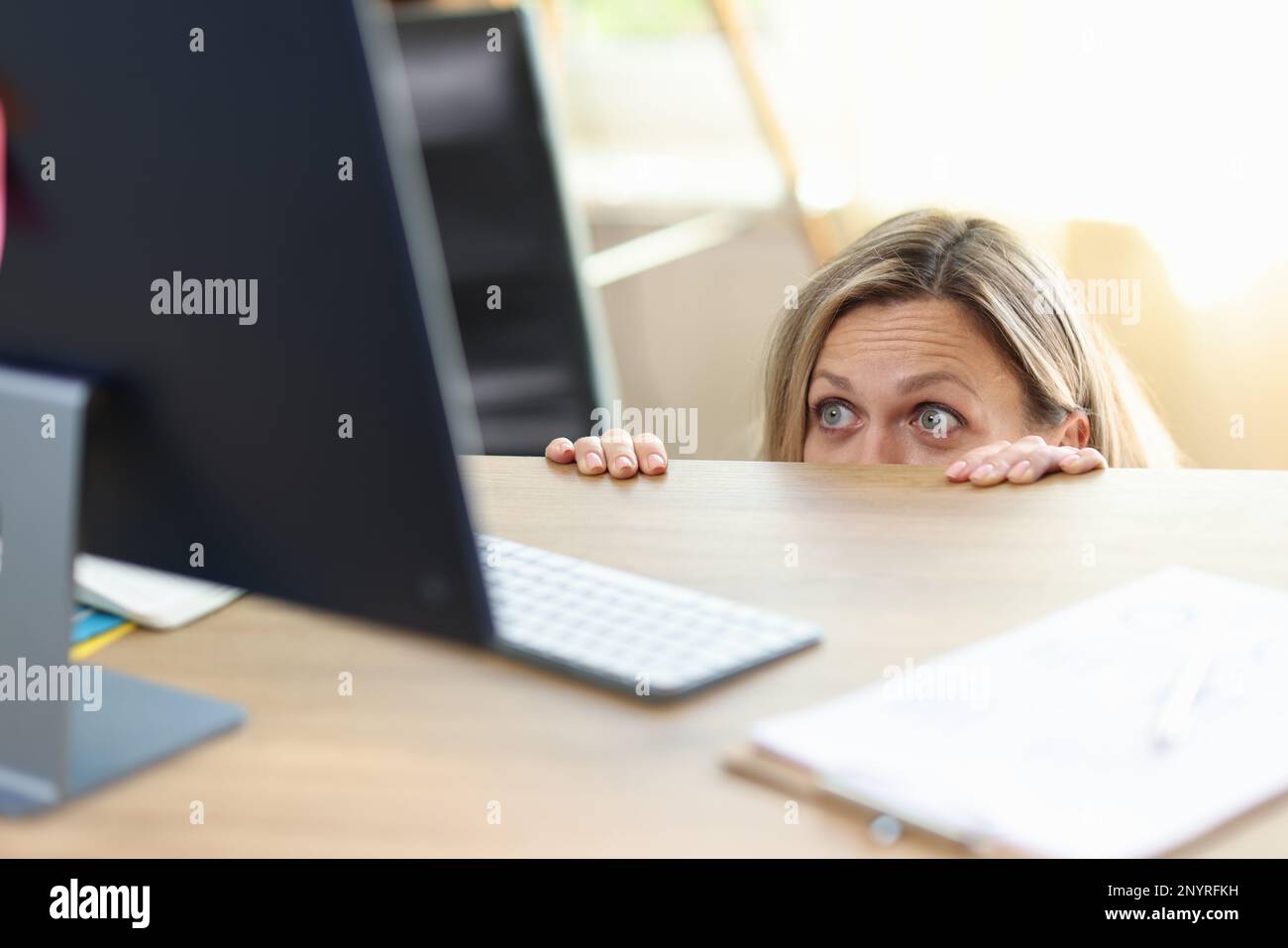 Surprised and excited female peeping out desk and looking at pc screen ...