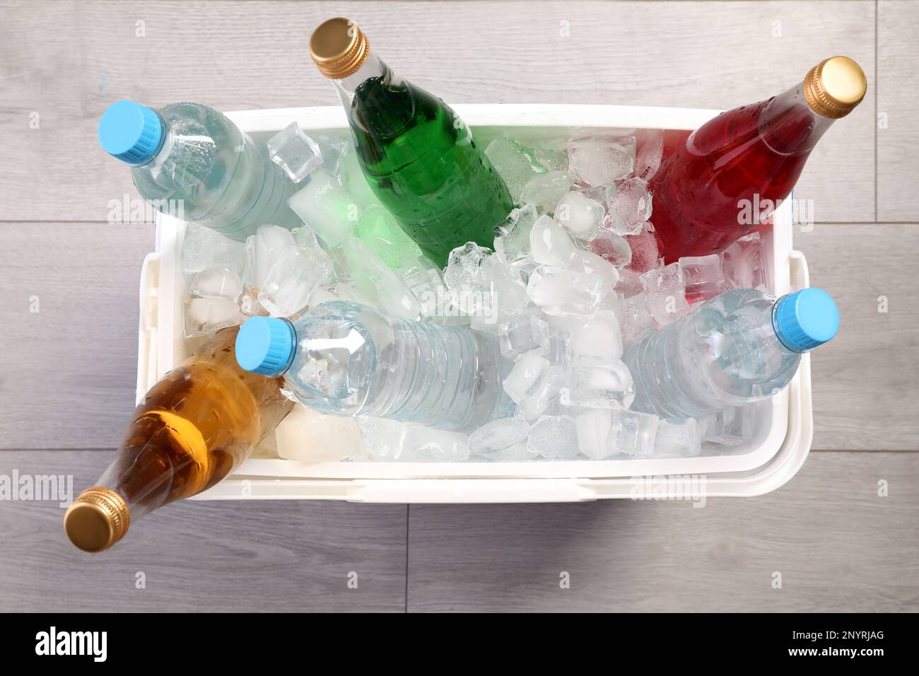 Plastic cool box filled ice cubes and refreshing drinks on wooden floor ...