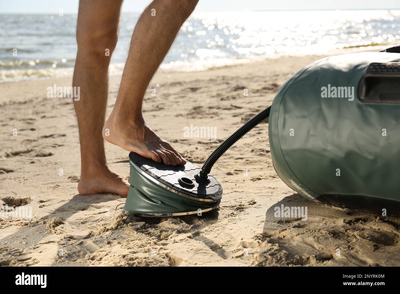 Man pumping inflatable rubber fishing boat at sandy beach on sunny day ...