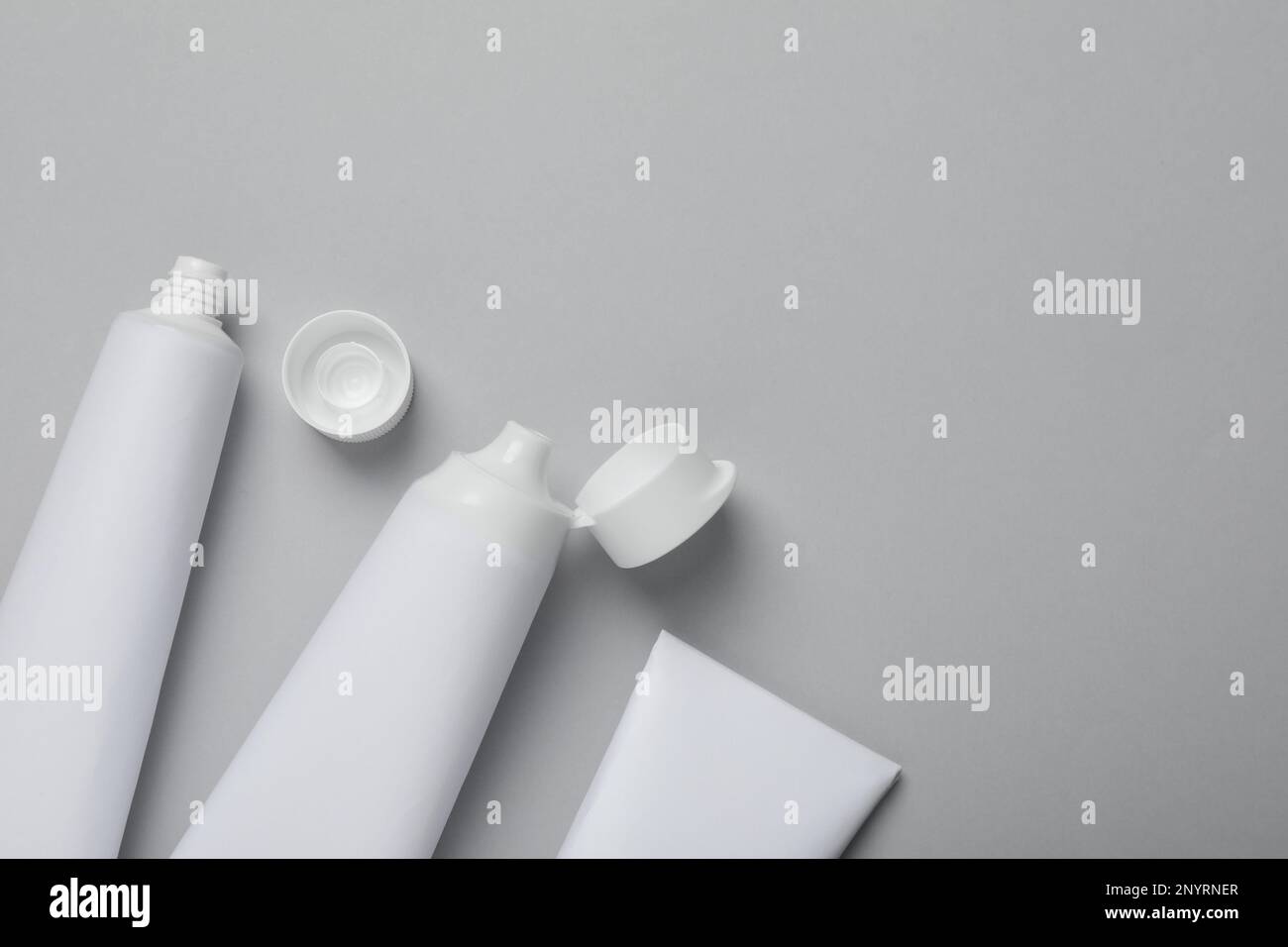 Blank tubes of toothpaste on light grey background, flat lay. Space for ...