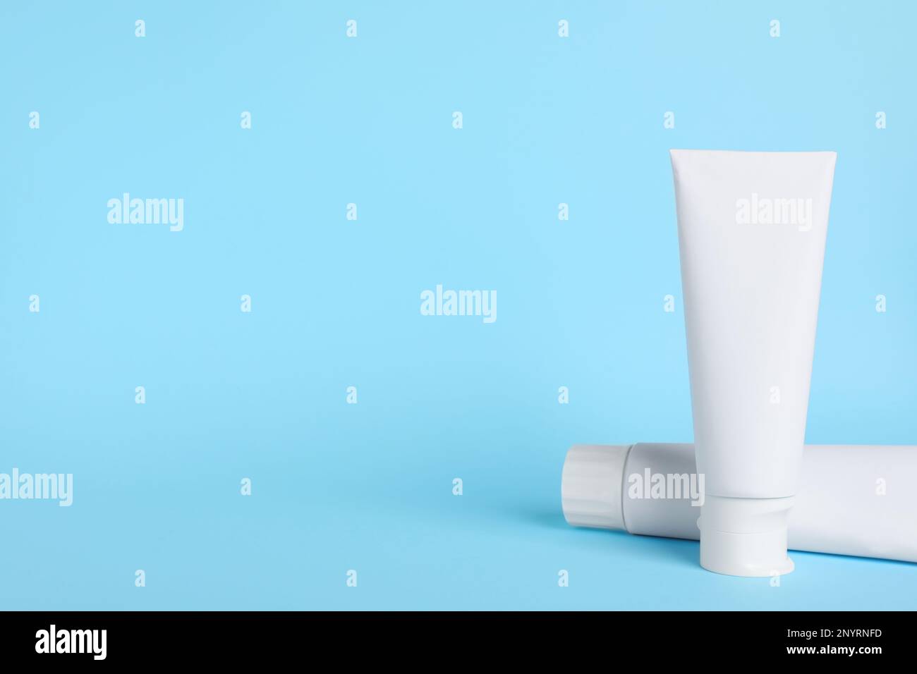 Blank tubes of toothpaste on light blue background. Space for text ...