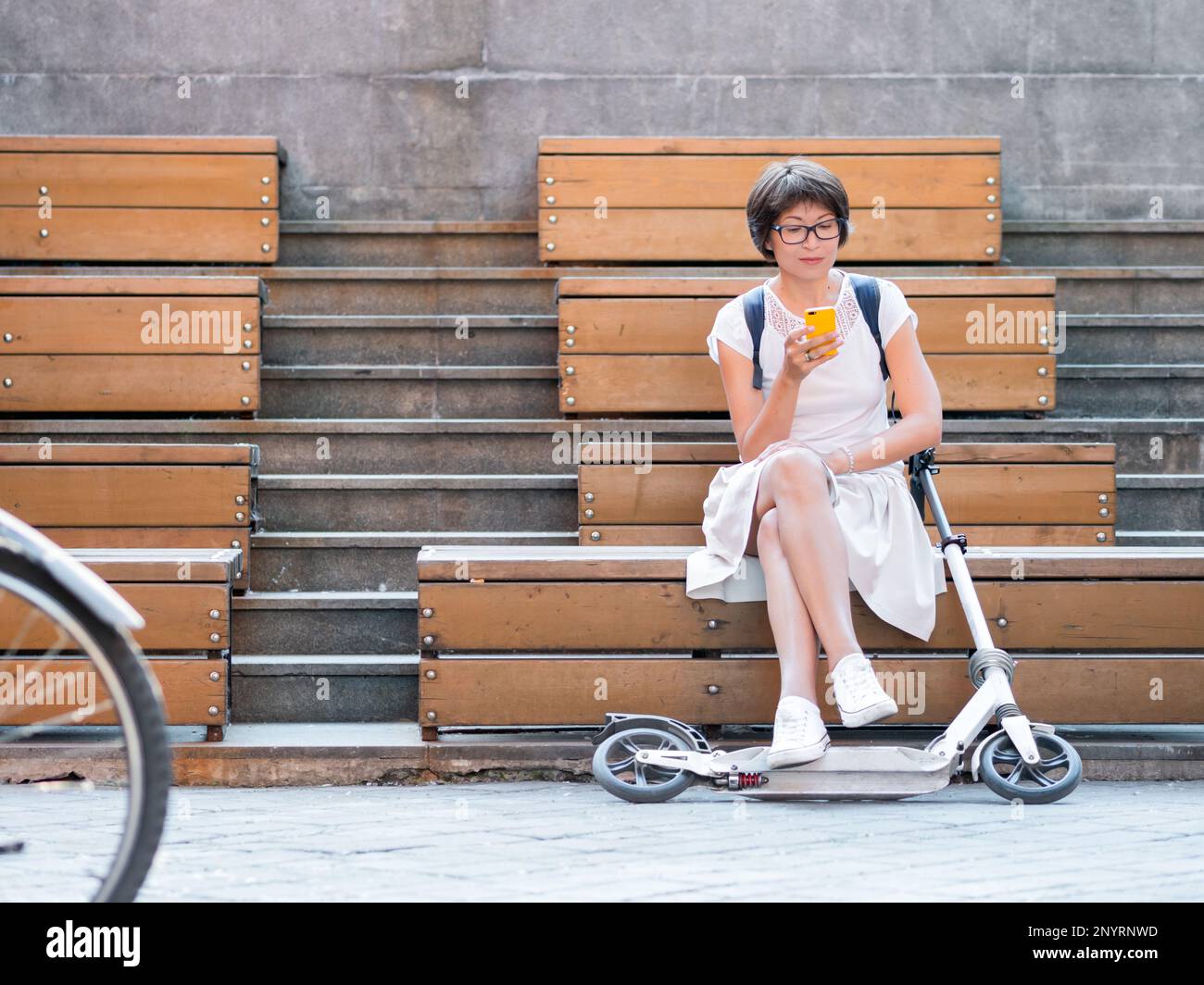 Woman sits on wooden bench and texting on her smartphone after riding ...