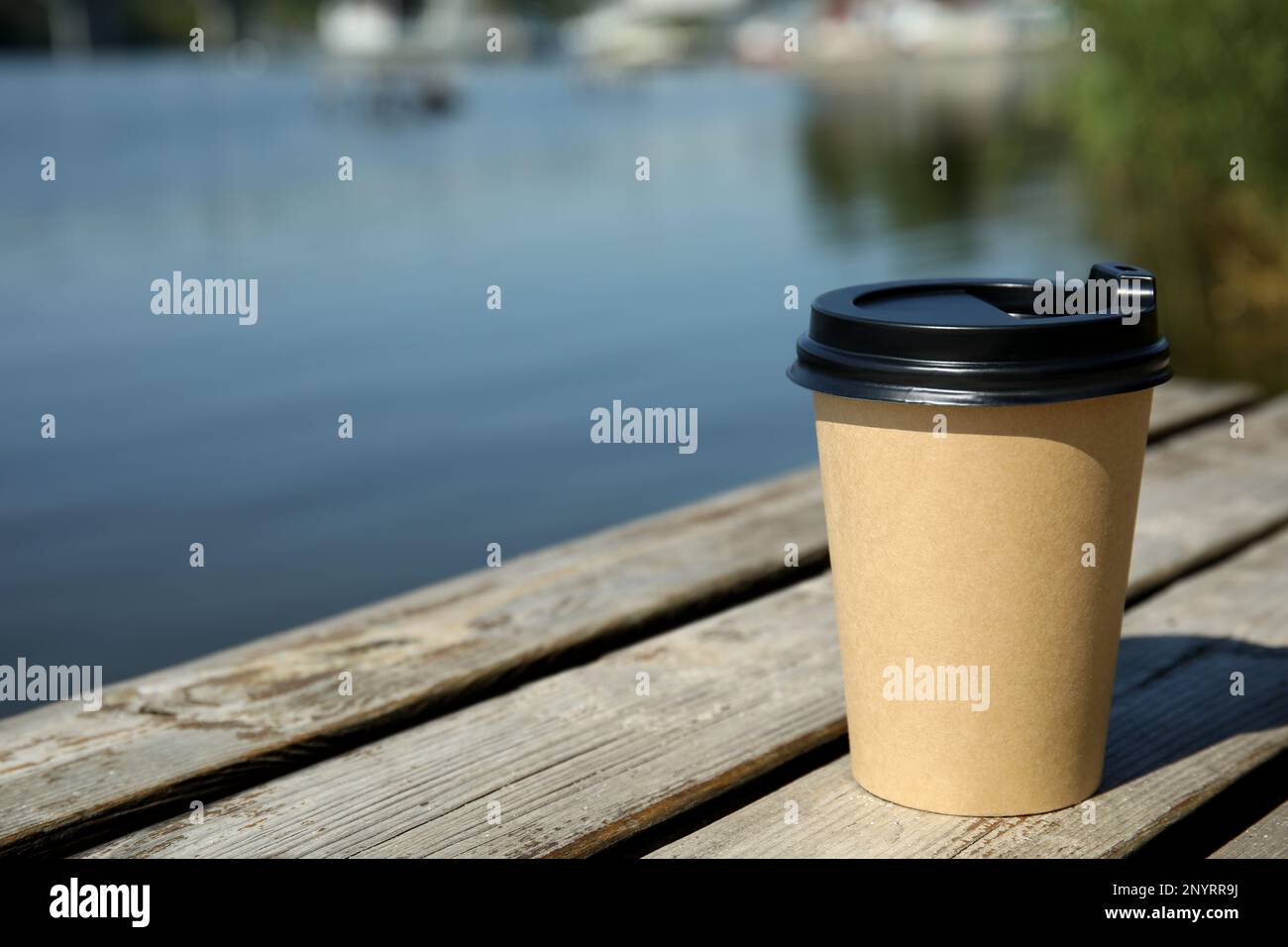 Takeaway cardboard coffee cup with plastic lid on wooden pier near ...