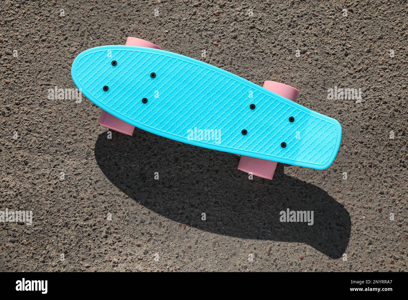Modern light blue skateboard with pink wheels on asphalt road outdoors ...