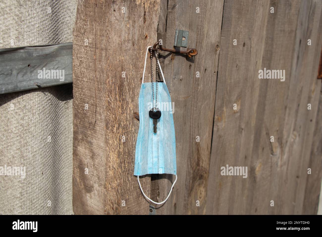 medical mask hanging on a hook and a door key on an old wooden gate in ...
