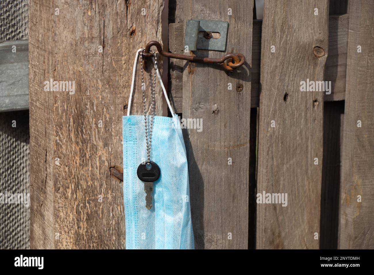 medical mask hanging on a hook and a door key on an old wooden gate in ...