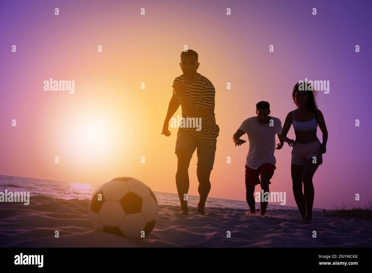 Friends playing football on beach at sunset Stock Photo - Alamy