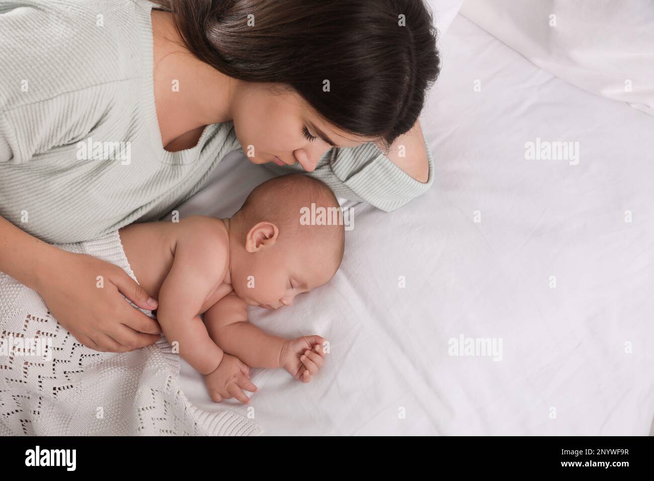 Young mother resting near her sleeping baby on bed, top view. Space for ...