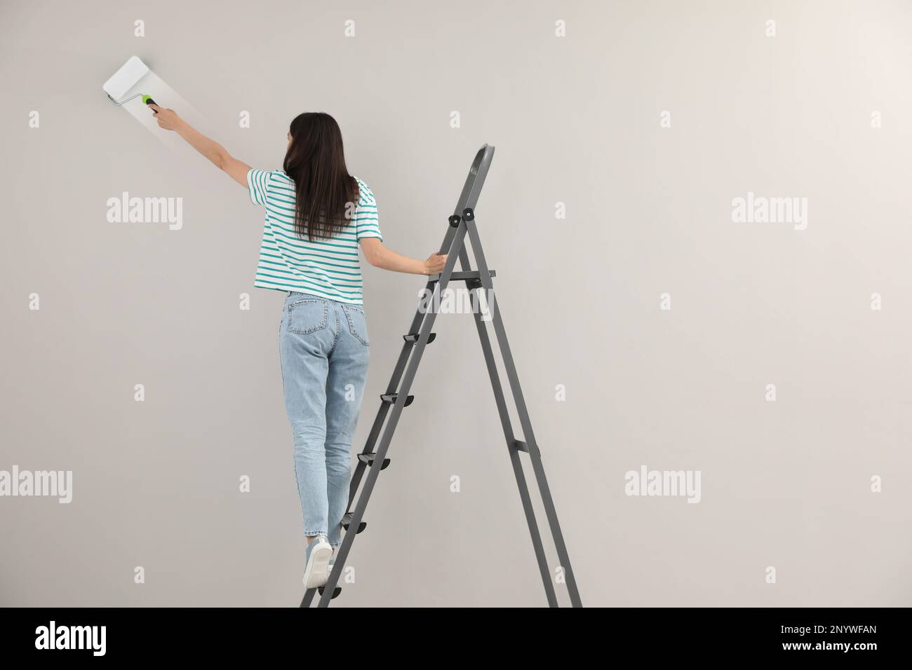Young woman painting wall with roller on ladder, back view Stock Photo ...