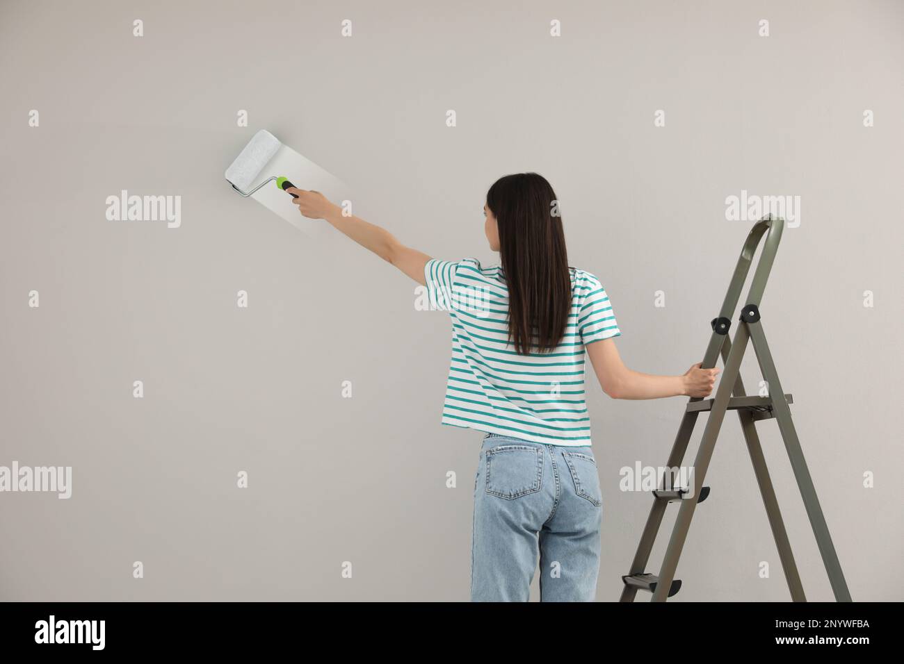 Young woman painting wall with roller on ladder, back view Stock Photo ...