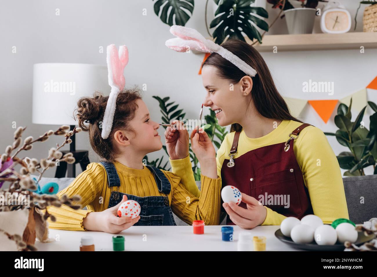 Funny young mom and happy little child daughter decorate eggs with ...